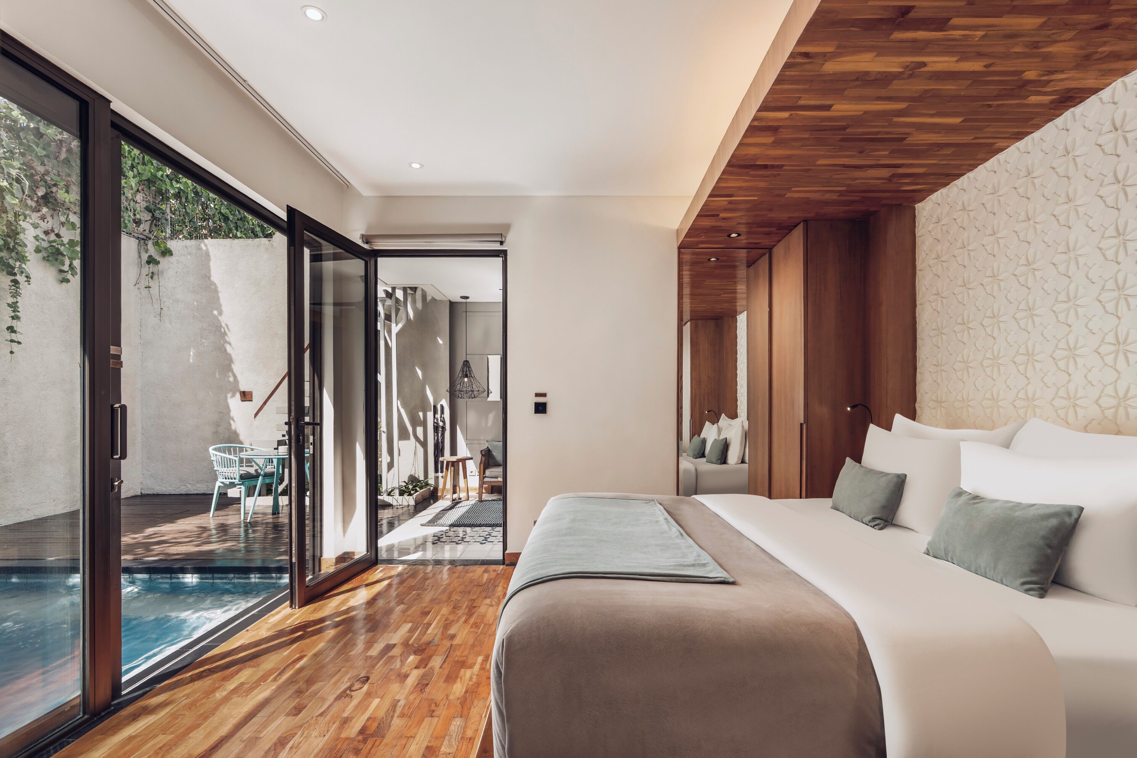 Quarto moderno com cama grande, teto de madeira e porta de correr de vidro que dá para uma área de piscina.