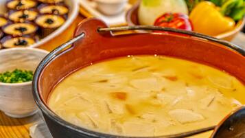 Uma tigela de sopa com alça, acompanhada por uma tigela de cogumelos, uma tigela de cebolinha e uma tigela de vegetais fatiados.