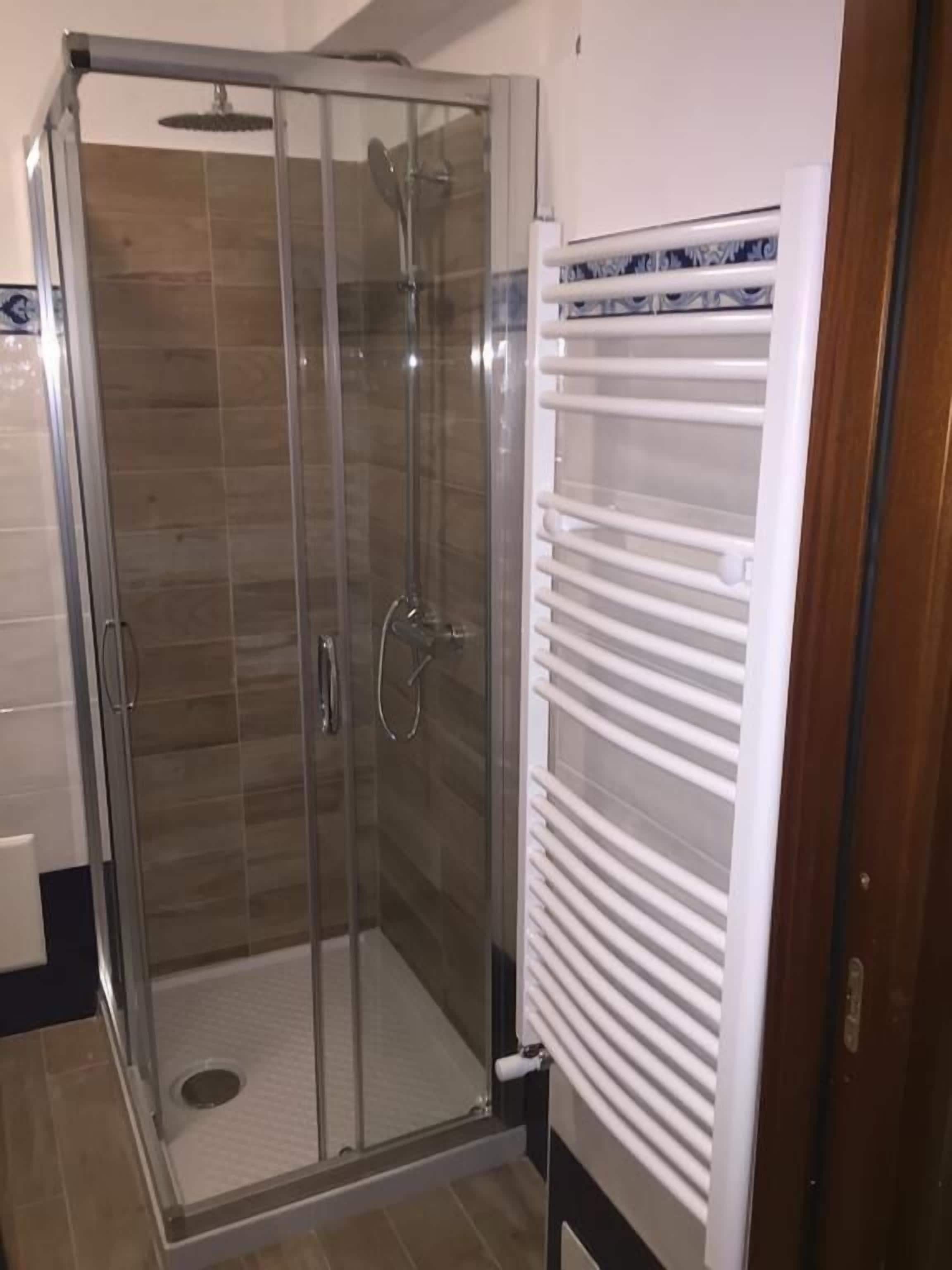 Uma área de chuveiro com paredes de vidro e um porta-toalhas branco ao lado.