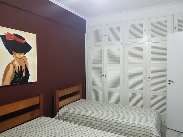 Quarto com duas camas, um guarda-roupa grande e um quadro na parede.