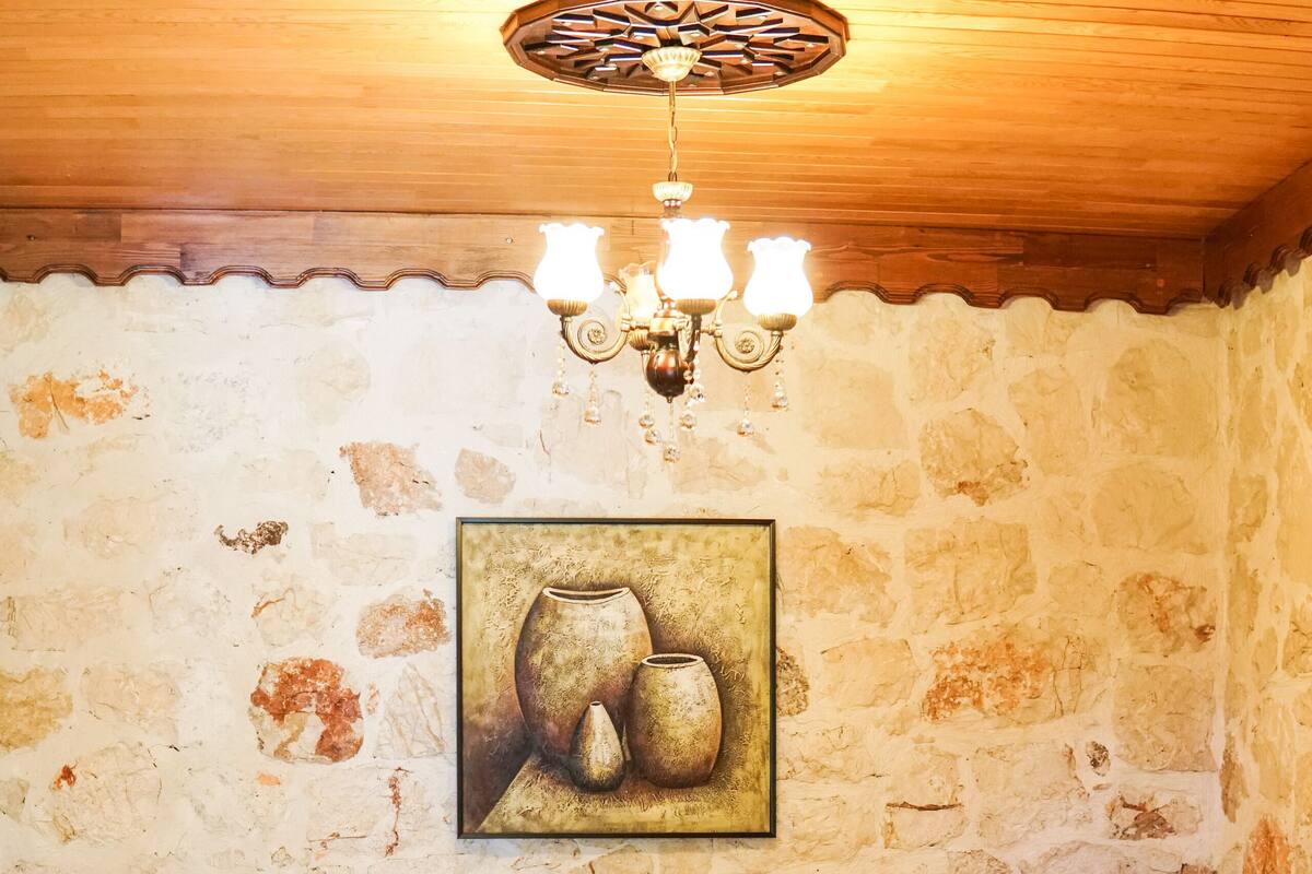 Quarto com duas camas, parede de pedra, teto de madeira, candelabro e telefone antigo.