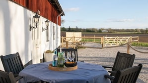 Uma área de refeições ao ar livre com uma mesa posta para dois, uma cadeira de madeira e uma garrafa de vinho.
