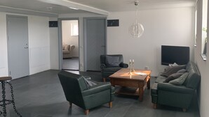 Uma sala de estar ampla com uma grande televisão de tela plana, dois sofás verdes, uma mesa de centro de madeira e um lustre.