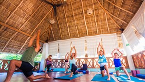 Um grupo de pessoas praticando yoga em um espaço com teto de colmo e vigas de madeira.