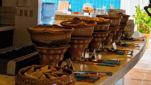 Bancada de cozinha com vasos de terracota, utensílios, um dispenser de água e um revestimento de azulejos azuis.