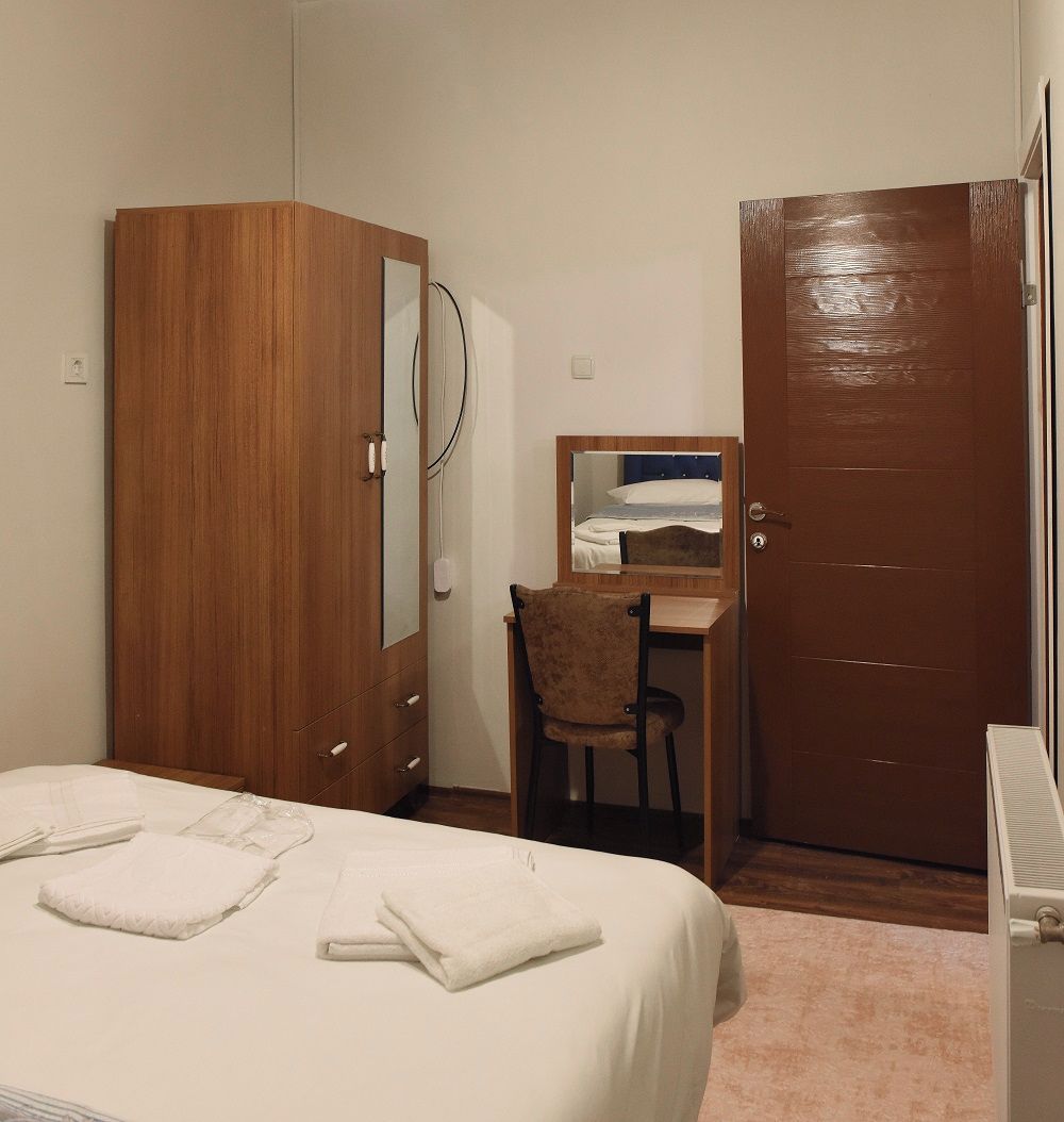 Quarto com cama, guarda-roupa de madeira, secretária e cadeira, além de uma porta.