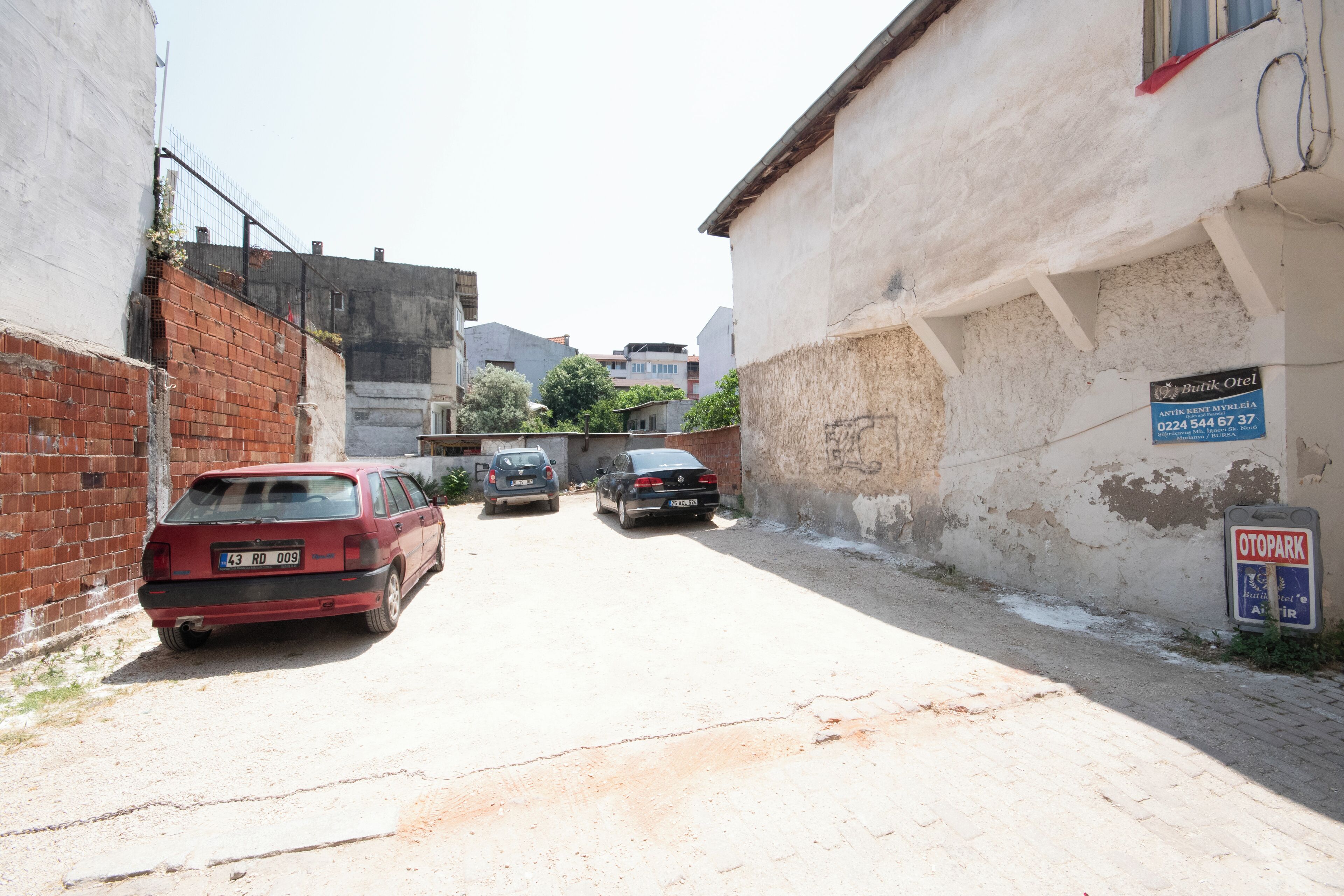 Rua estreita com carros estacionados e um prédio com placa indicando um estabelecimento comercial.