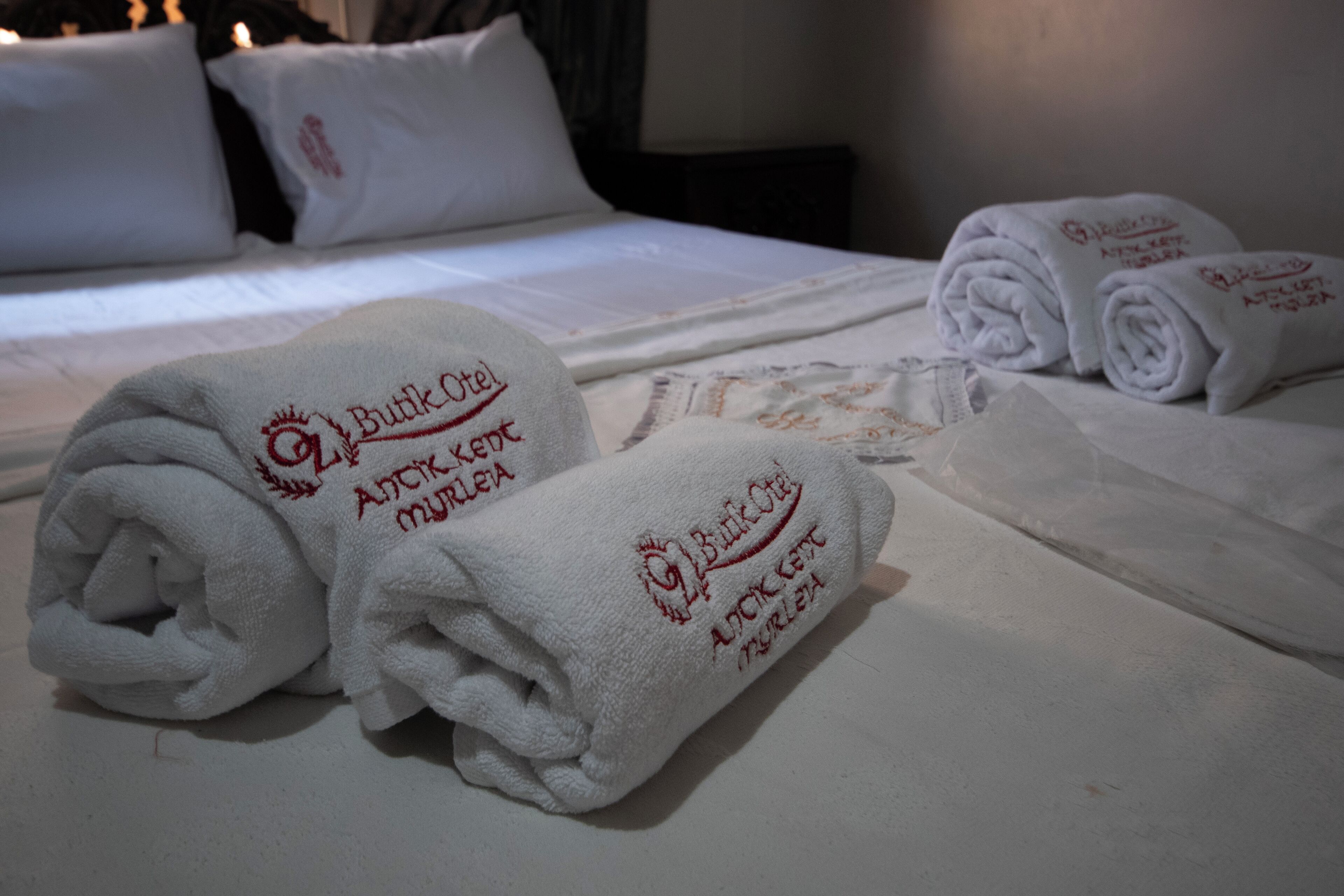 Cama bem arrumada com lençóis brancos e toalhas dobradas, decoradas com bordado.