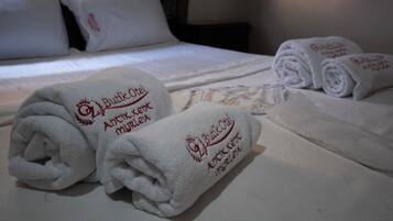 Cama bem arrumada com lençóis brancos e toalhas dobradas, decoradas com bordado.