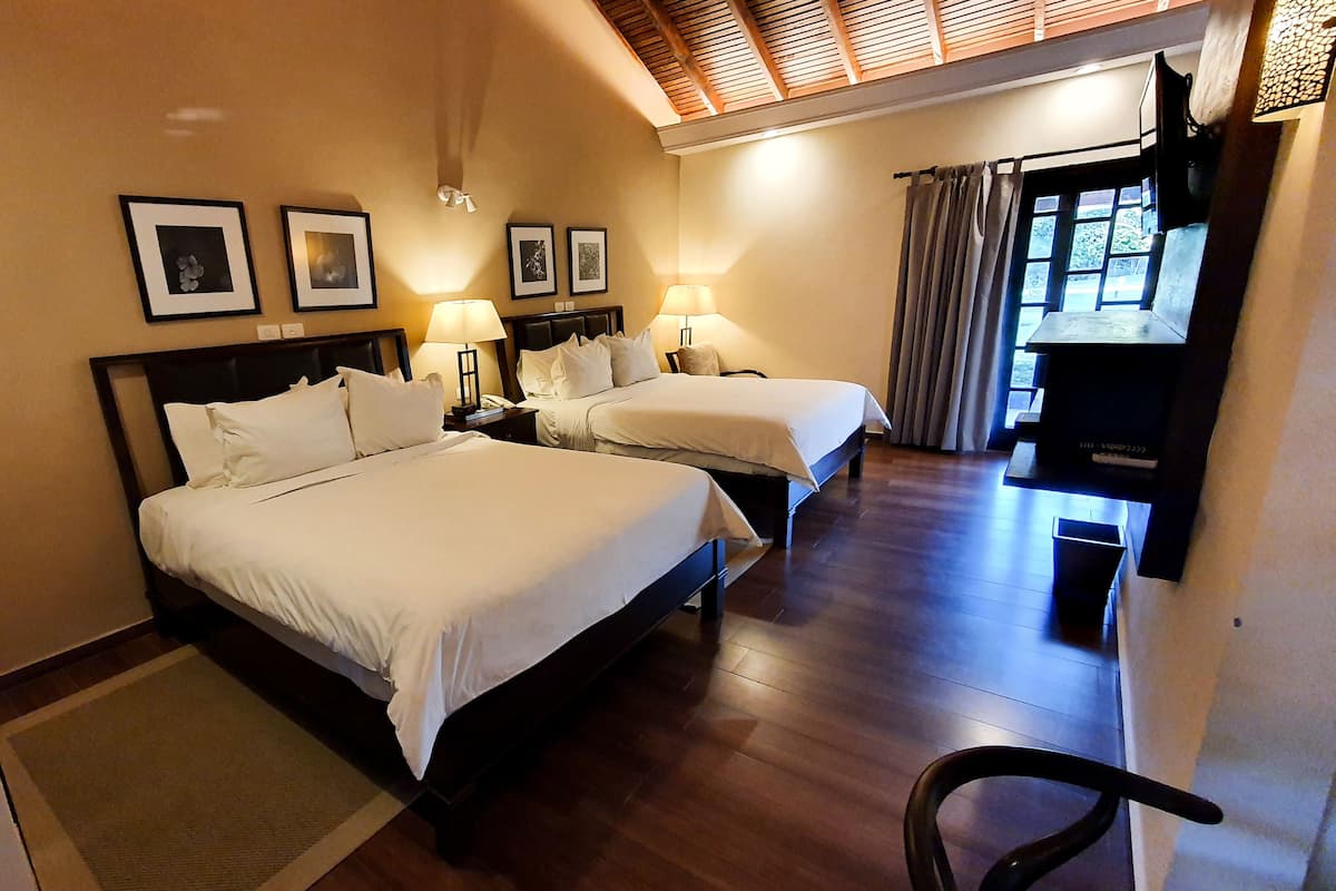 Quarto de hotel com duas camas, uma escrivaninha, uma cadeira e uma televisão.