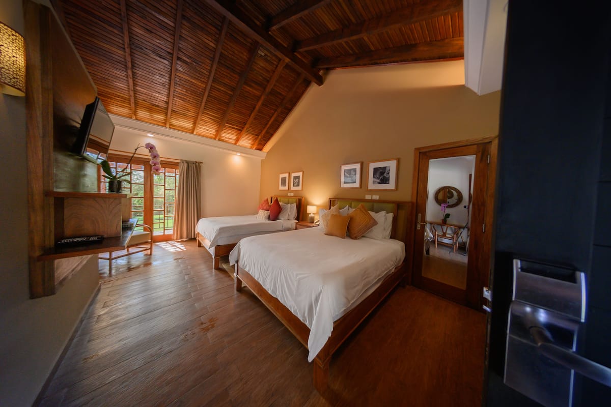 Quarto com duas camas, soalho de madeira, uma televisão sobre uma estante e uma porta que dá para outro cômodo.