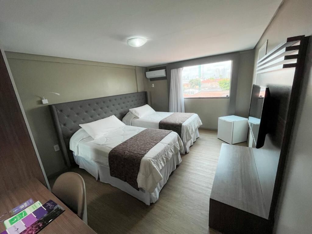 Quarto de hotel com duas camas, uma escrivaninha e uma televisão.
