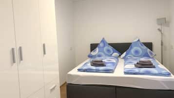Quarto com cama, duas almofadas, mesa de cabeceira e guarda-roupa.