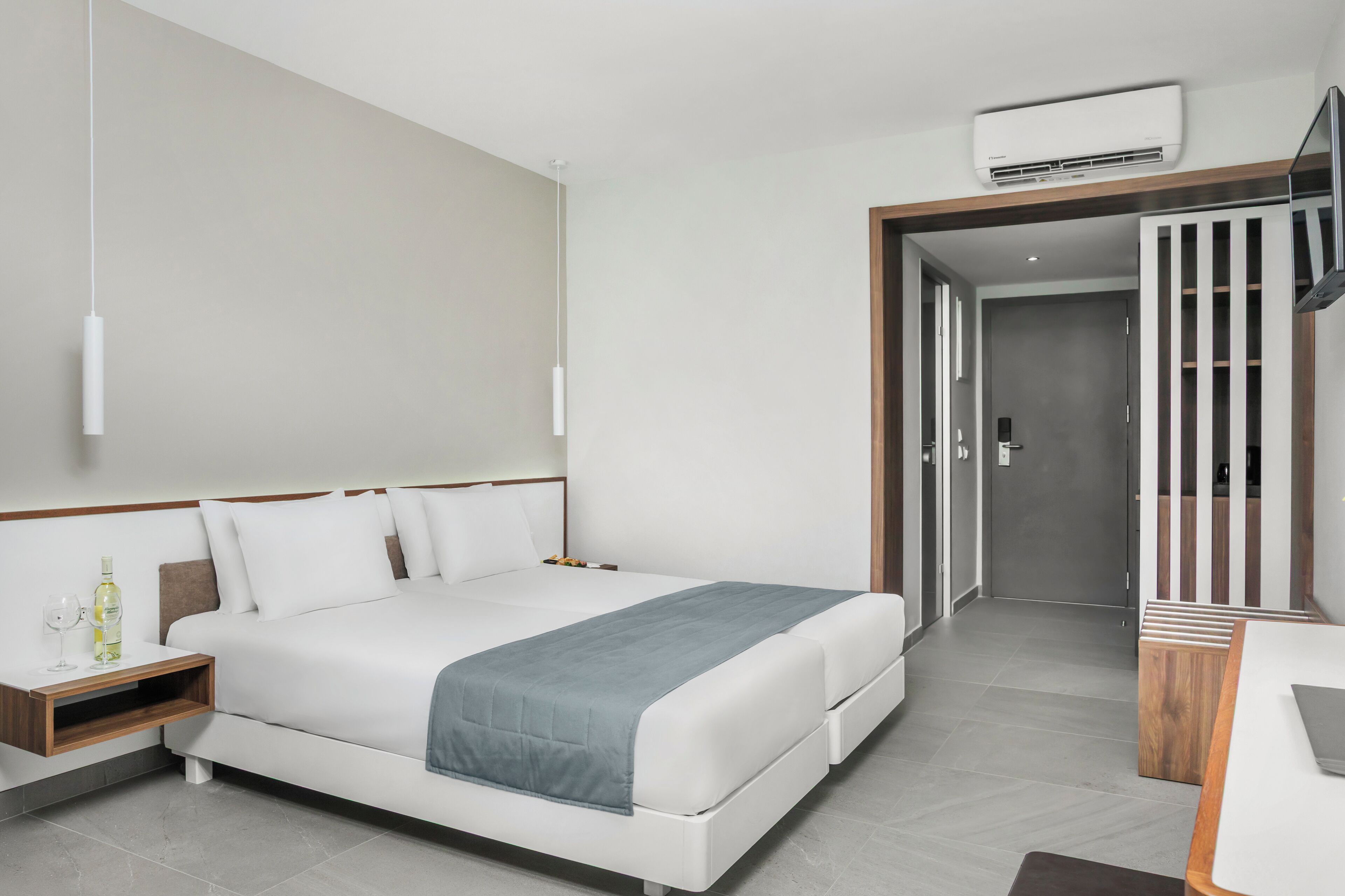 Quarto de hotel moderno com uma cama grande, mesa de cabeceira com um copo de vinho, escrivaninha com um laptop e porta deslizante para um banheiro.