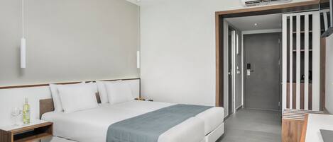 Quarto de hotel moderno com uma cama grande, mesa de cabeceira com um copo de vinho, escrivaninha com um laptop e porta deslizante para um banheiro.
