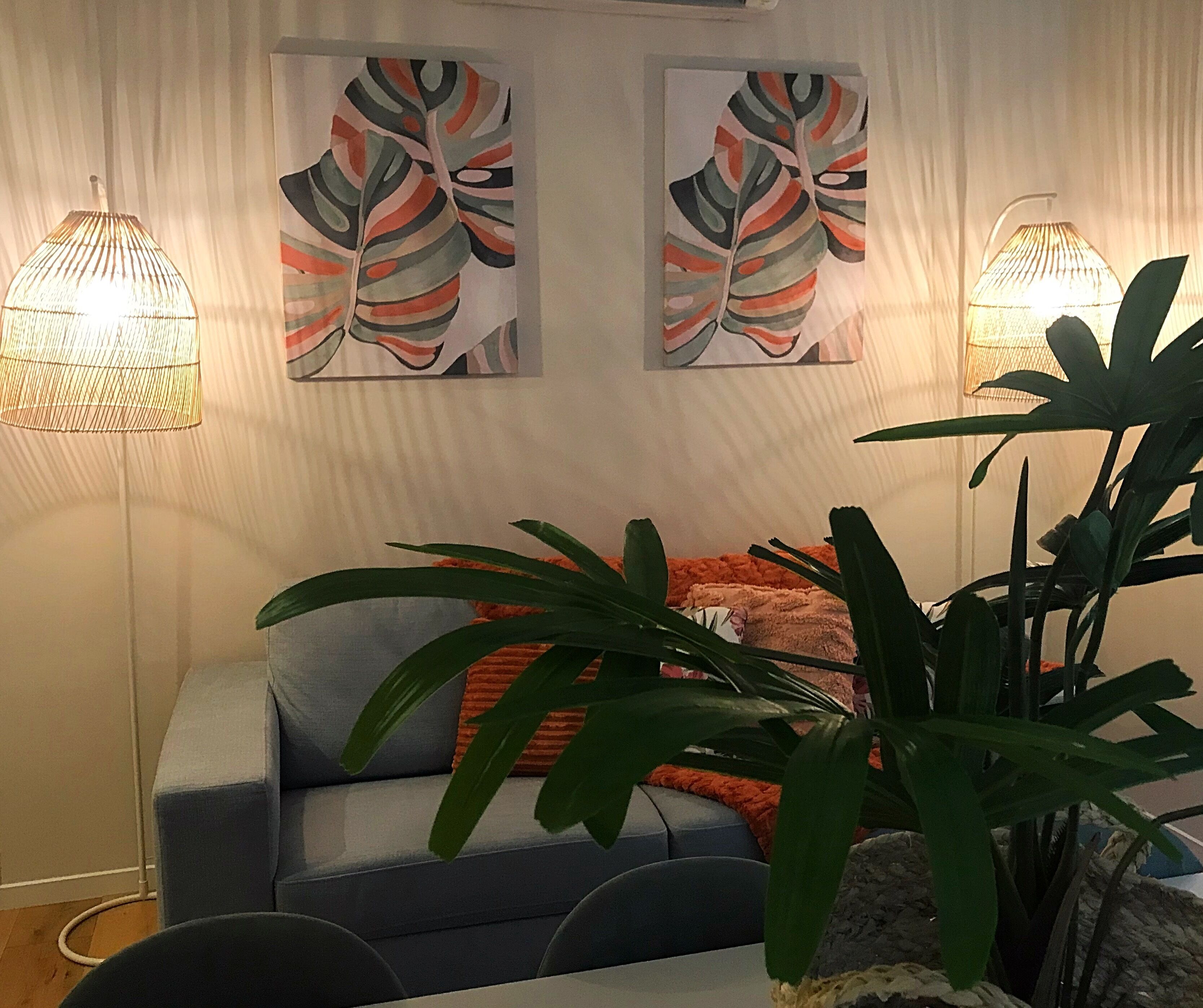 Uma sala de estar moderna com um sofá, duas pinturas abstratas e uma planta grande.