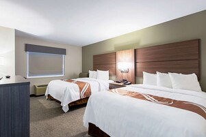 Quarto de hotel com duas camas, uma escrivaninha e uma janela.