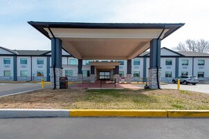 Entrada coberta a um edifício com fachada de pedra, um banco e um contentor de lixo.