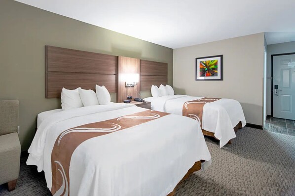 Quarto de hotel com duas camas, uma mesa de cabeceira, um abajur e um quadro na parede.