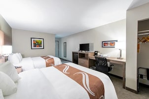 Quarto de hotel com duas camas, uma mesa, uma cadeira, televisão e obras de arte nas paredes.