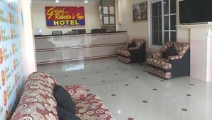Uma área de recepção de hotel com sofás estampados, um balcão de recepção e uma grande tela de televisão.