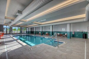 Piscina interior com pistas demarcadas, elevador de piscina e área ensolarada com vista para o exterior.