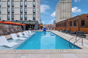 Piscina com espreguiçadeiras e guarda-sóis, rodeada por edifícios.