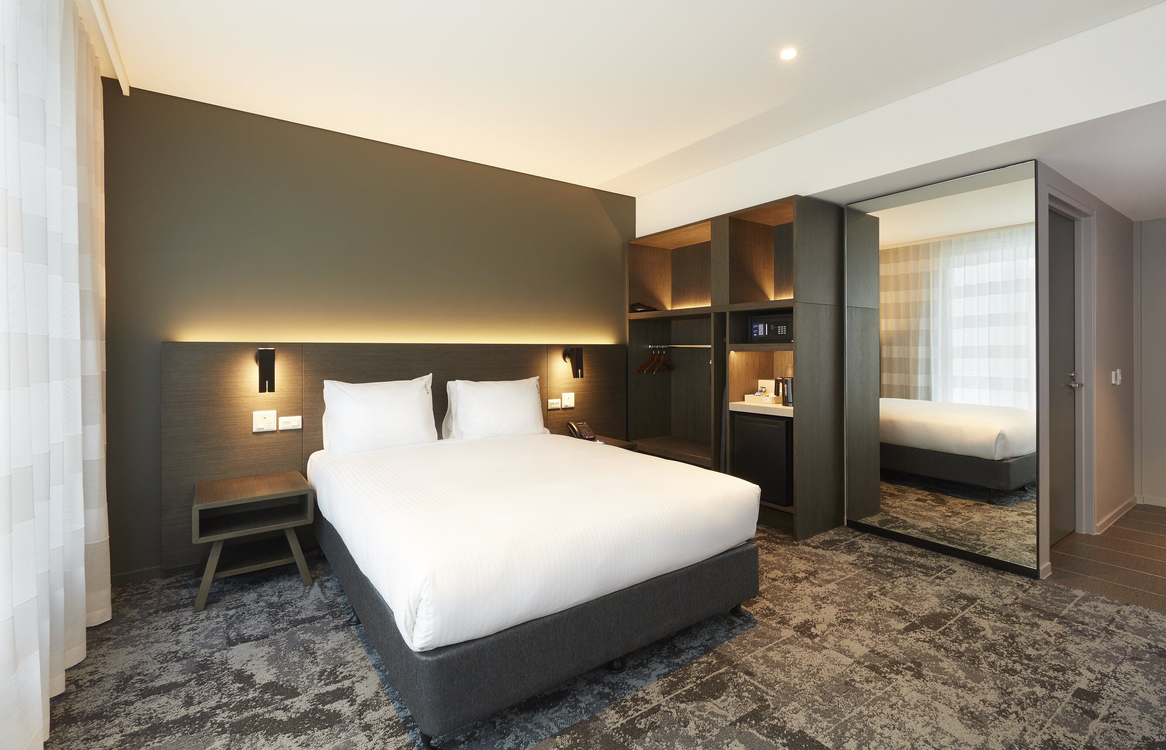 Quarto de hotel moderno com uma cama grande, mesas de cabeceira, um guarda-roupa e um espelho.