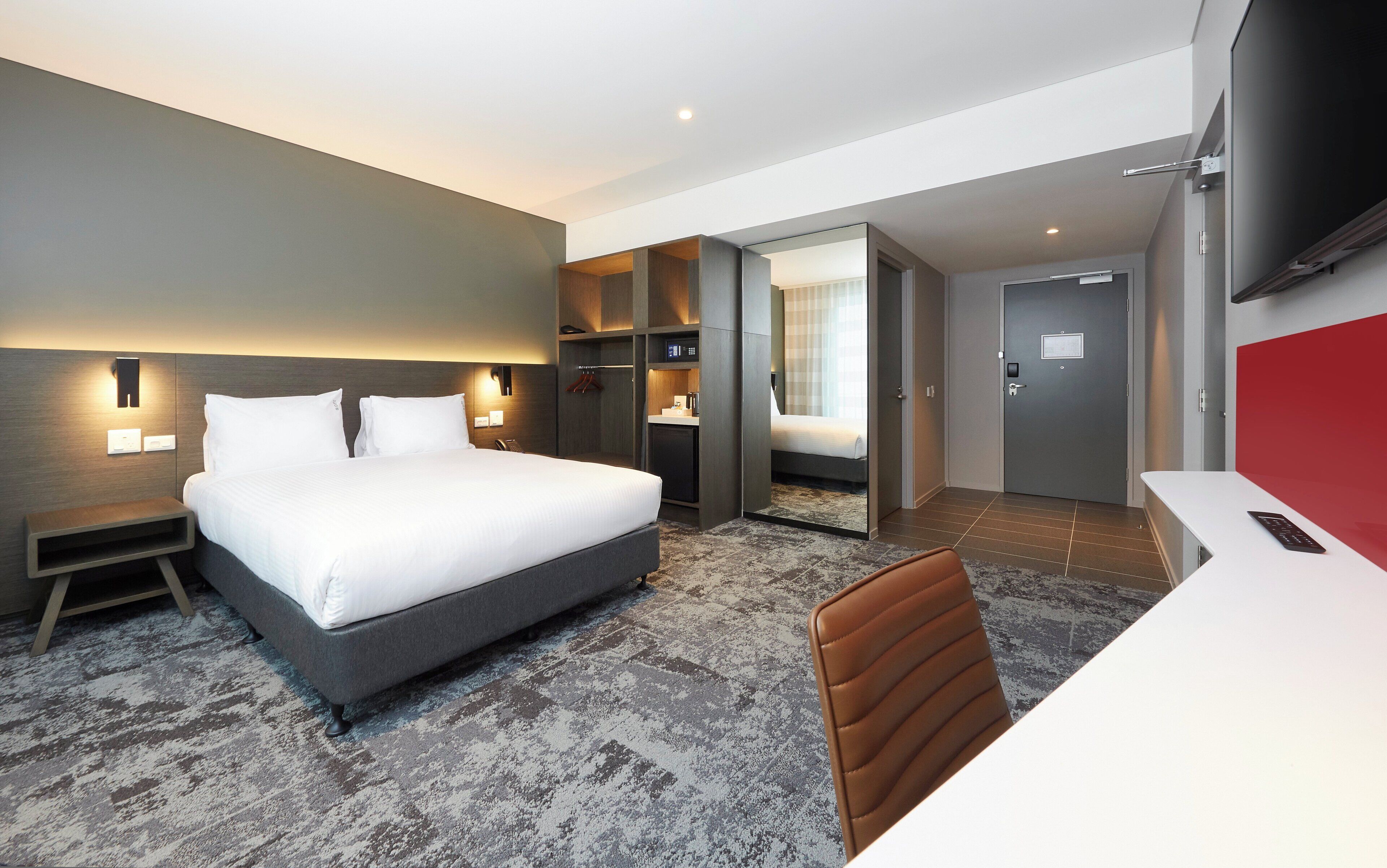 Quarto de hotel moderno com uma cama grande, mesas de cabeceira, escrivaninha e televisão.