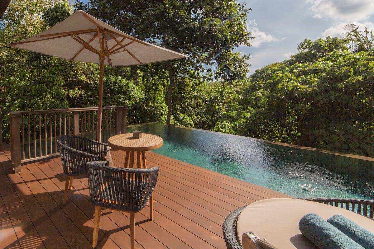 Um deck de madeira com piscina, rodeado por vegetação exuberante.