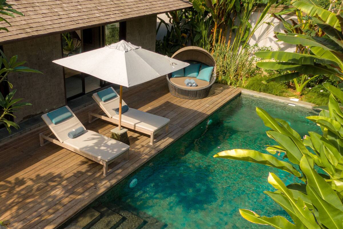 Uma área à beira da piscina com espreguiçadeiras e uma mesa sob um toldo.