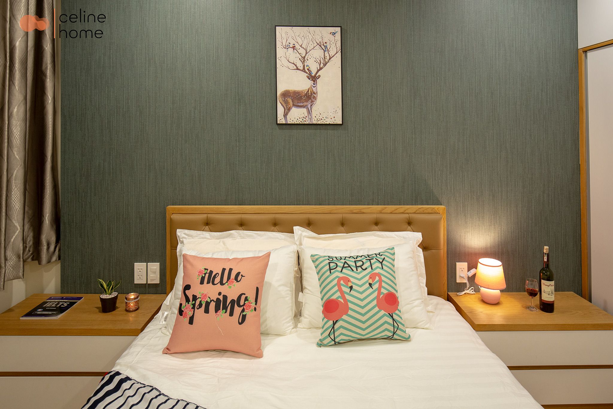 Uma cama bem arrumada com duas almofadas decorativas, uma mesinha de cabeceira com uma luminária e um frasco, e uma obra de arte emoldurada na parede.