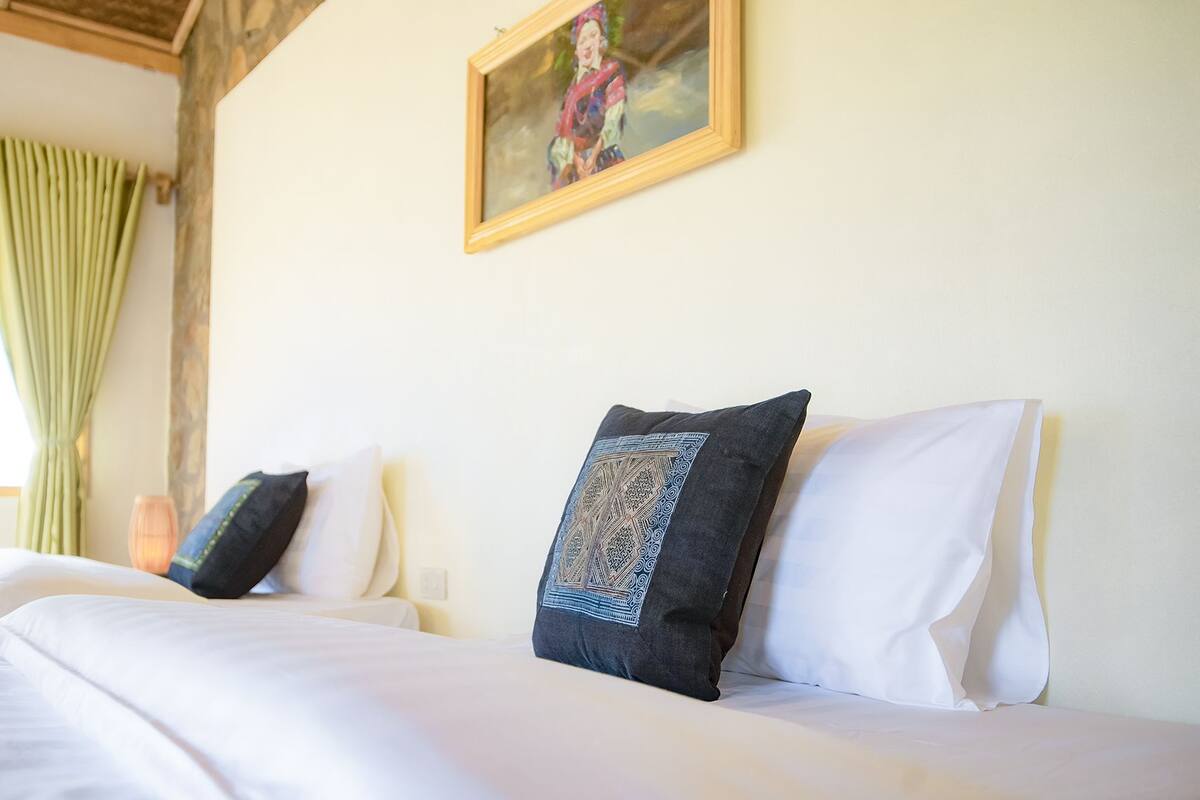Quarto de hotel com duas camas, um quadro na parede e uma janela com cortinas verdes.