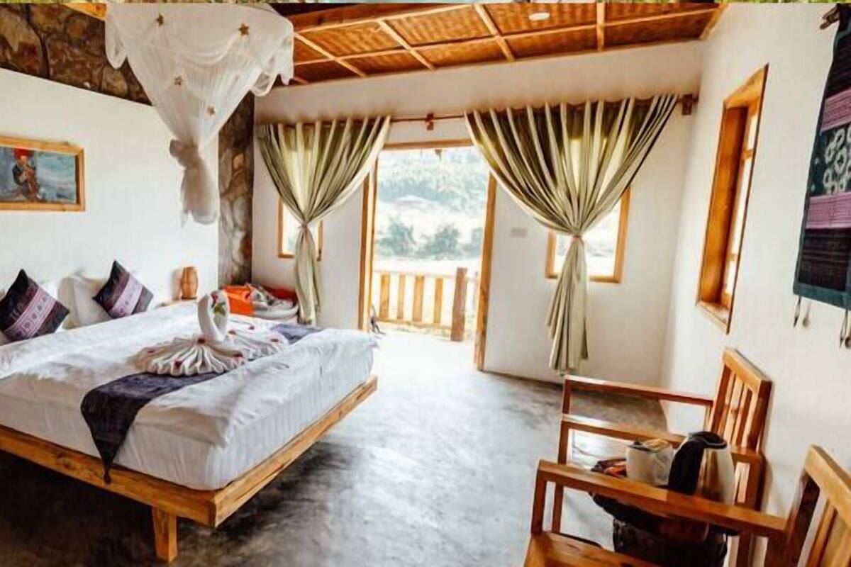 Quarto com cama de madeira, mesa de cabeceira, cadeira e janela com cortinas.