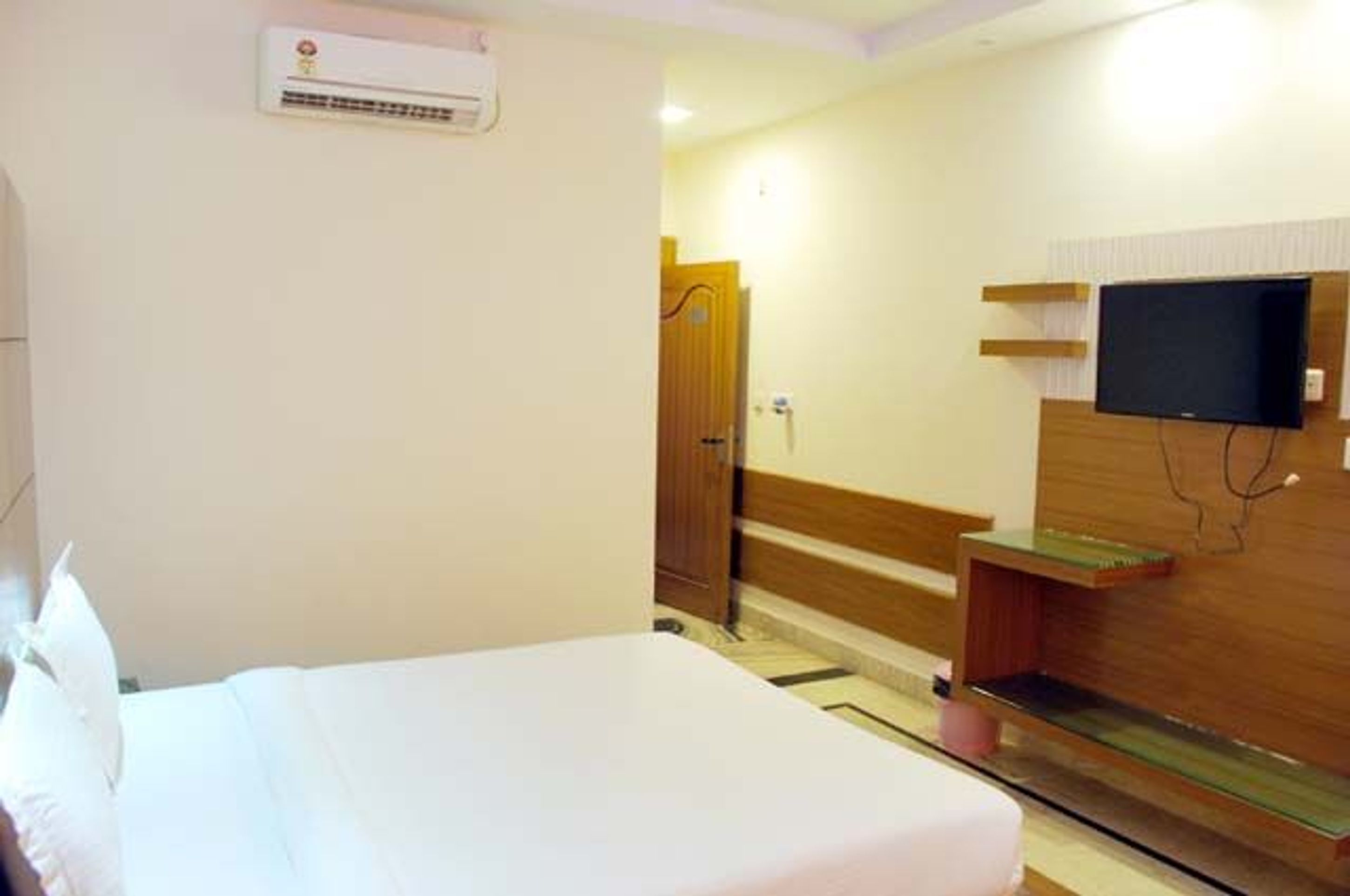 Quarto de hotel com uma cama, uma TV fixada na parede, um banco de madeira e um aparelho de ar condicionado.