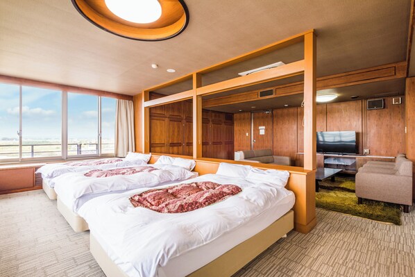 Quarto de hotel com duas camas, televisão, sofá e uma janela grande com vista.