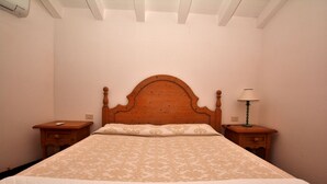 Quarto com cabeceira de madeira, colcha estampada, duas mesas de cabeceira com abajures e parede branca.