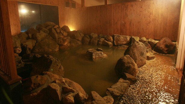Interior de madeira com área de fontes termais rodeada por rochas.