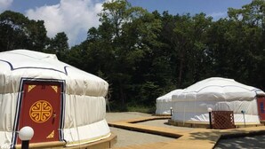 Uma fileira de yurts brancas com portas vermelhas, com árvores e um céu claro ao fundo.