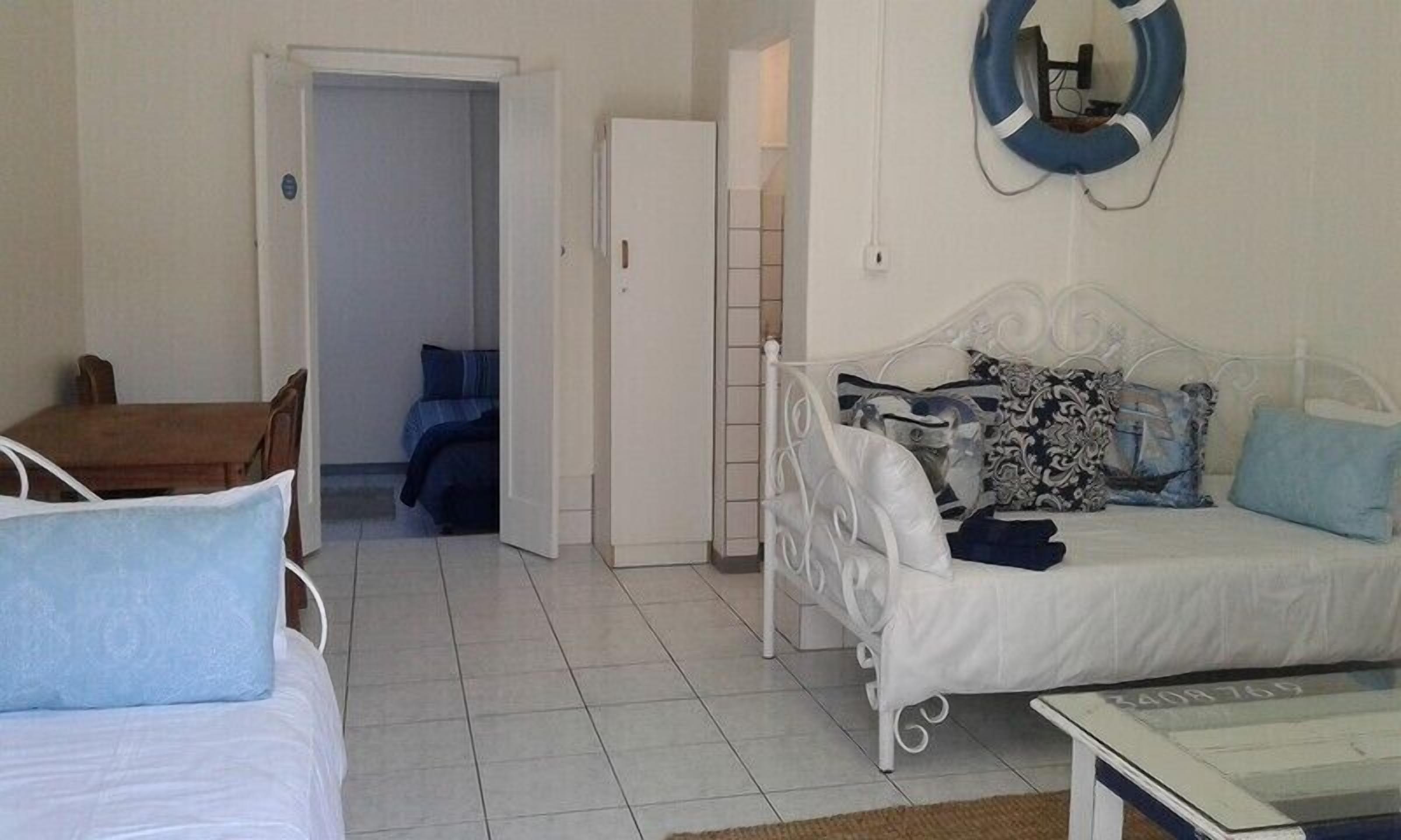 Quarto com cama, mesa e cadeira. Uma porta dá acesso a outro cômodo.