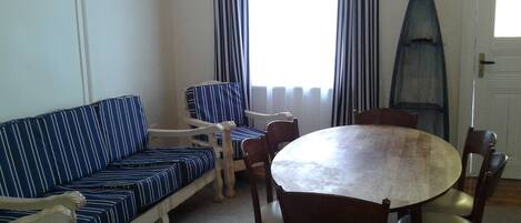 Um quarto com um sofá listrado, uma mesa redonda com cadeiras e uma janela com cortinas.