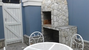 Uma lareira de pedra ao ar livre com um fornalho azulejado, rodeada por uma parede azul e um portão branco.
