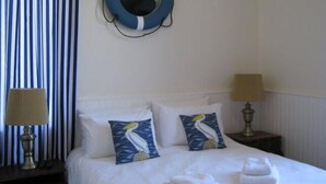Quarto de hotel com uma cama, duas almofadas com desenho de pássaro, um círculo de flutuação na parede e cortinas listradas.