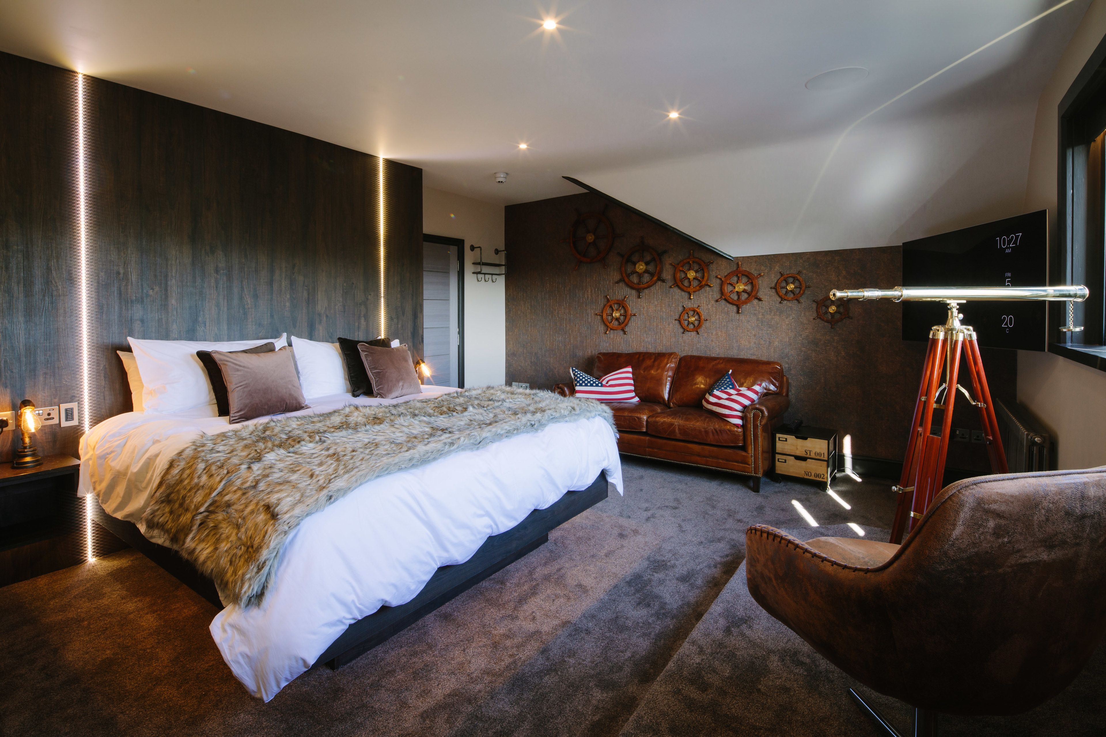 Quarto moderno com cama grande, sofá de couro e escada de madeira.