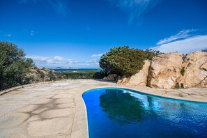 Uma piscina com borda curva, cercada por ladrilhos de pedra e uma grade de metal.