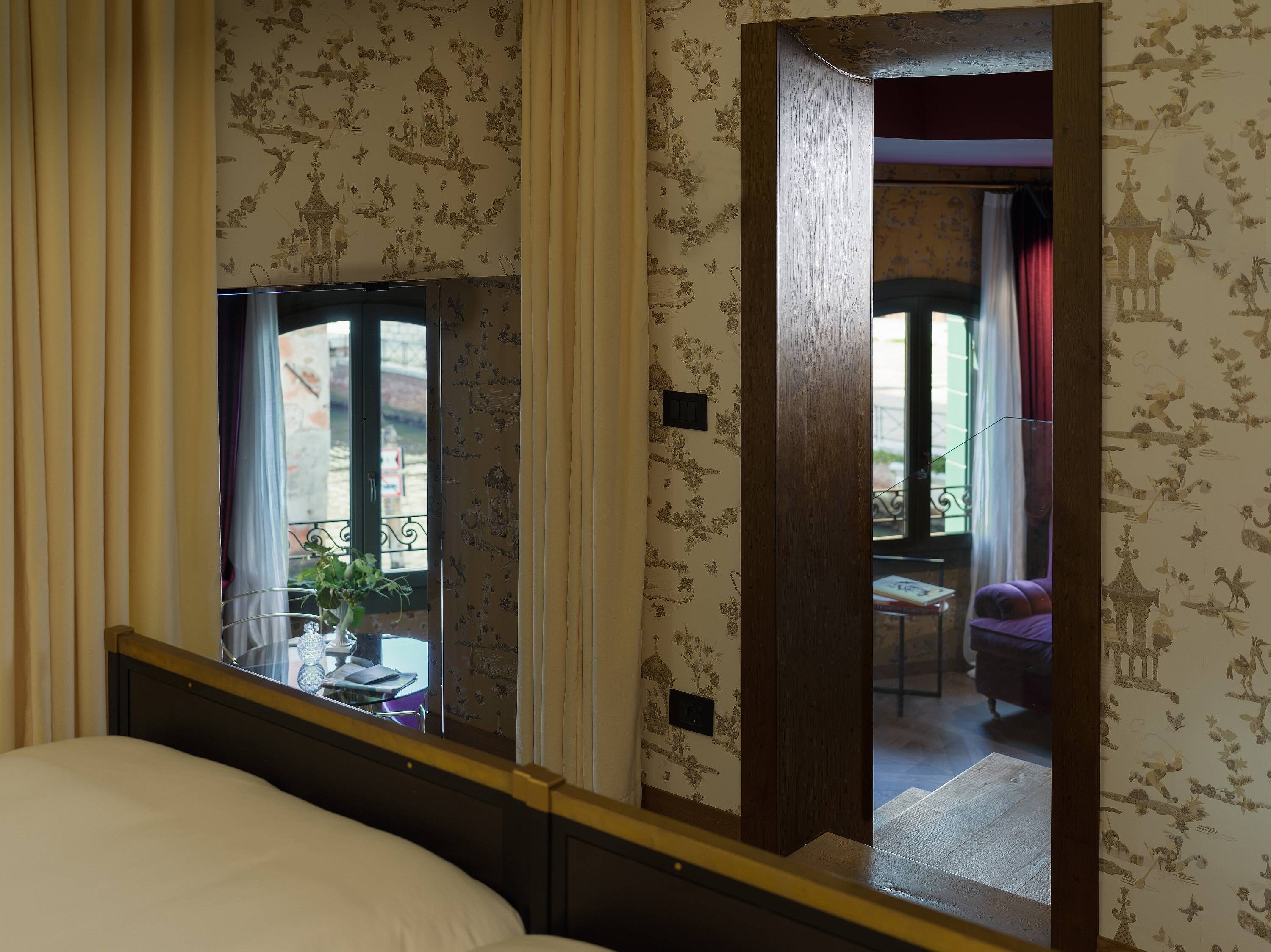 Quarto de hotel com cama, janela com cortinas, espelho e vista para a varanda externa.