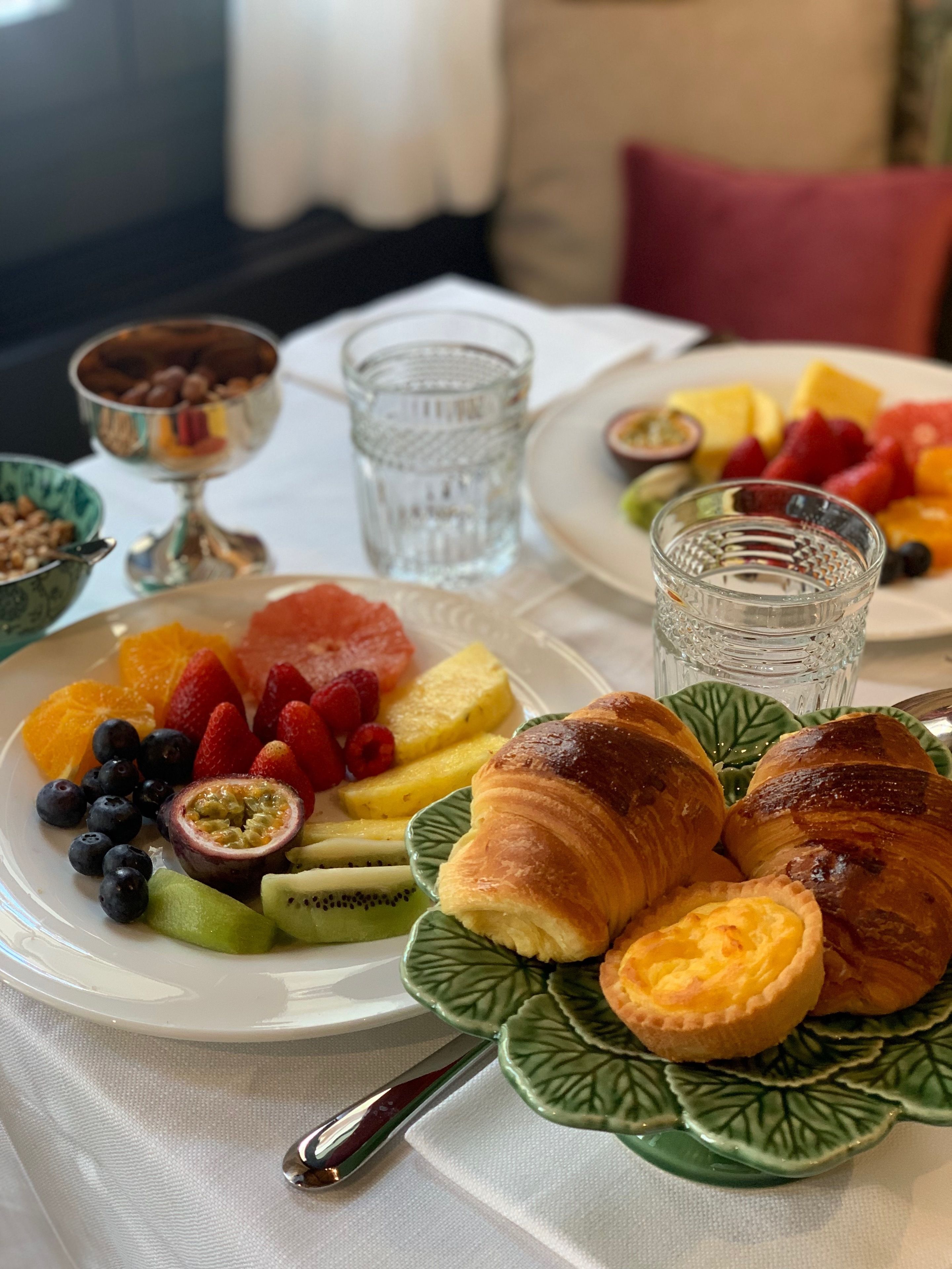Uma mesa de café da manhã com pratos de frutas, doces e uma pequena tigela de nozes.