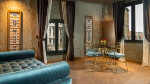 Quarto com sofá azul, mesa de jantar com quatro cadeiras e vista para edifícios através de uma janela com cortinas.