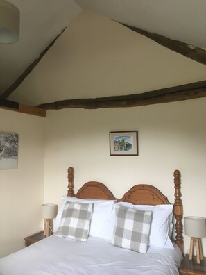 Quarto com estrutura de cama de madeira, roupa de cama branca e um quadro na parede.