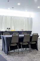 Uma sala de conferências com uma mesa comprida, seis cadeiras e um serviço de buffet com pratos, copos e temperos.